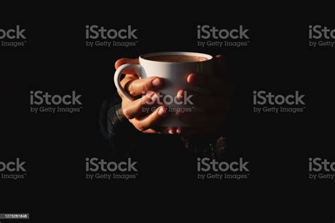 검은 색 배경에 커피의 흰색 컵을 들고 여성의 손 어둠 속에서 뜨거운 음료의 찻잔에 그녀의 손을 따뜻하게 여자 최소한의 스타일