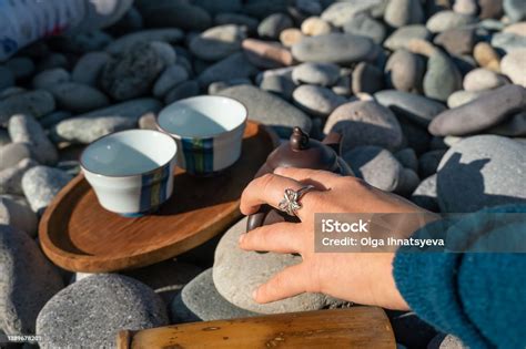 화창한 날씨에 바다의 조약돌 해변에서 중국 전통 다도 손으로 점토 주전자를 만지는 한 여성의 클로즈업 근처의 나무 쟁반에 두