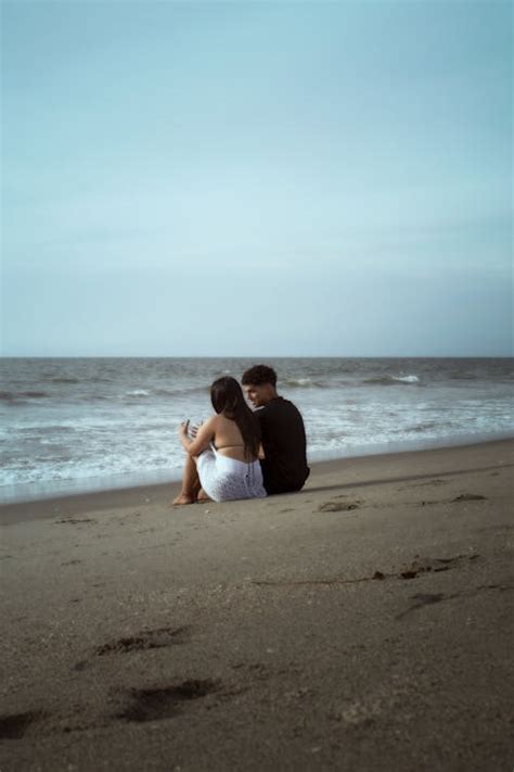 일몰 무렵 모래사장에 앉아 있는 로맨틱한 커플 · 무료 스톡 사진