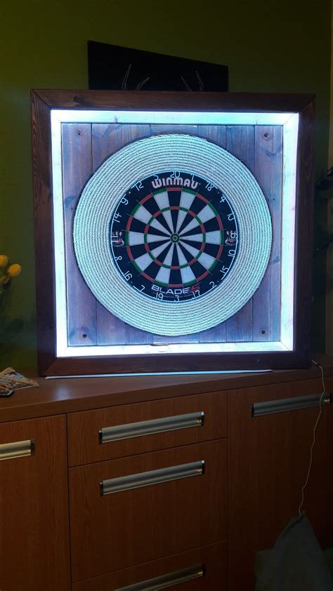 A Lighted Dart Board On Top Of A Wooden Cabinet In Front Of A Television Screen