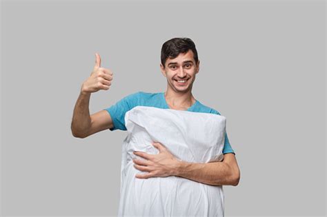 젊은 브루넷 남자 Shwoing 엄지 손가락 을 들고 흰색 베개 고립 위에 회색 배경 가리키기에 대한 스톡 사진 및 기타 이미지