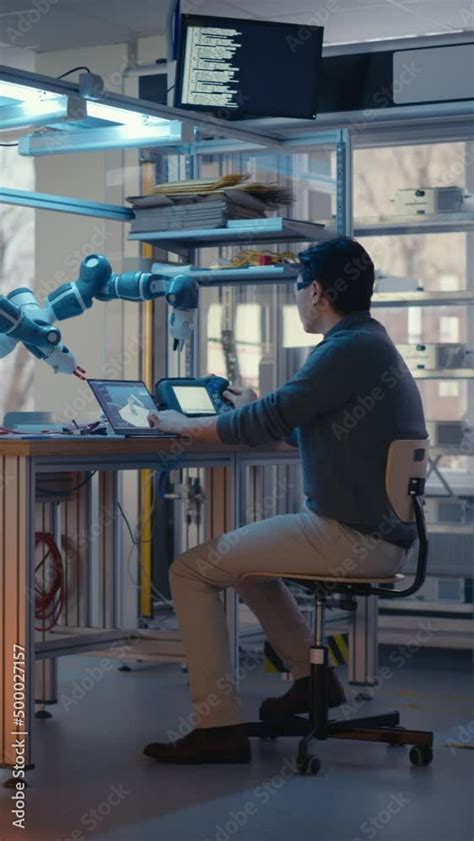 Professional Young Developer Coding At Laptop And Manipulate Of Robot Arm At Factory Workshop