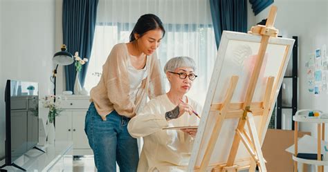 행복한 아시아 가족 딸이 가르치는 것은 캔버스에 화려한 작품을 그리는 나이 든 어머니를 즐기며 주말에는 집에있는 거실에서 함께