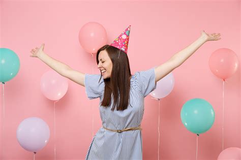웃 고 생일 모자와 파란 드레스 핑크 배경과 화려한 공기 Baloons에 손을 확산에 닫힌된 눈으로 젊은 여자의 초상화 생일