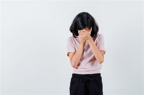 분홍색 티셔츠와 검은 색 바지에 손으로 얼굴을 덮고 피곤해 보이는 어린 소녀 무료 사진