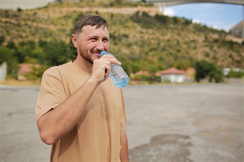 수염을 기른 자신감 넘치는 젊은 잘생긴 남자가 플라스틱 병에서 물을 마시고 더운 여름날 산의 경치를 즐기고 있다 의료 개념입니다 건강한 생활 습관 상쾌한 음료 남자에 대한