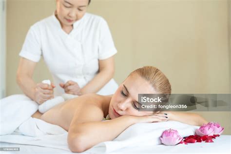 흰색 스파 침대에 누워 젊은 백인 여성 전문 태국 안마사에 의해 스파 살롱에서 Poultice 뜨거운 허브 마사지 뜨거운 압축