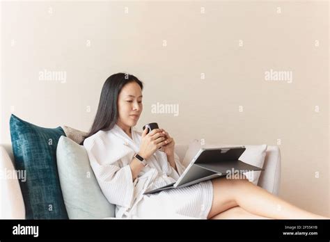 Woman In Dressing Gown Sit On Couch Holding Coffee While Working On