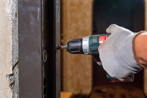 목수는 벽의 구멍을 뚫고 금속 도어 프레임에 드릴을 하고 나중에 나사를 나사로 나사로 고정하고 도어 프레임을 벽에 고정시합니다 가정용 장비에 대한 스톡 사진 및 기타 이미지