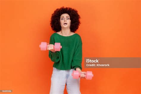 아프로 헤어 스타일을 가진 열심히 일하는 여성은 아령이있는 이두근을 입고 중장비를 키우기에서 얼굴을 찡그린다 20 24세에 대한 스톡 사진 및 기타 이미지 Istock