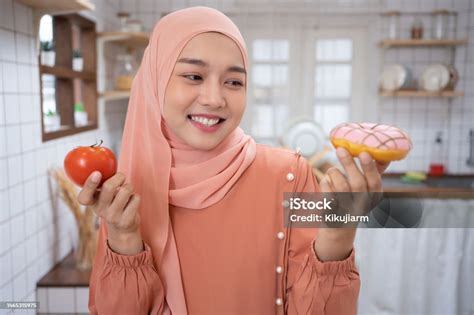 건강한 식생활 음식 개념 건강에 해로운 도넛과 유기농 빨간 토마토를 비교하는 무슬림 여성 부엌에서 생각 여자에 대한 스톡 사진