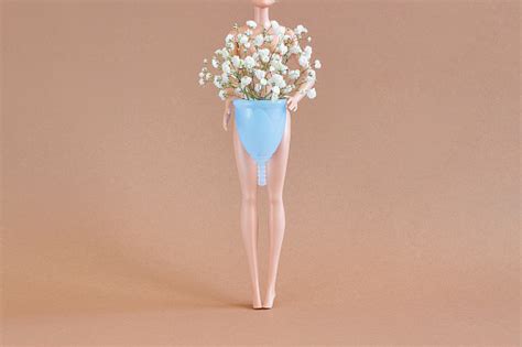 여성 인형은 복사 공간이있는 갈색 배경에 꽃다발이 섬세한 꽃과 함께 파란색 생리컵을 들고 있습니다 여성 친밀한 위생 여성 건강 개념 환경 친화적 인 제로 폐기물 대안 0명에