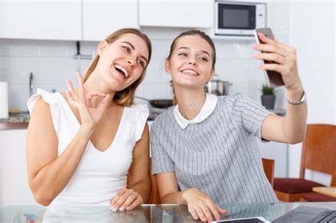 Two Young Girlfriends Making Selfie By Phone And Smiling At Table Stock