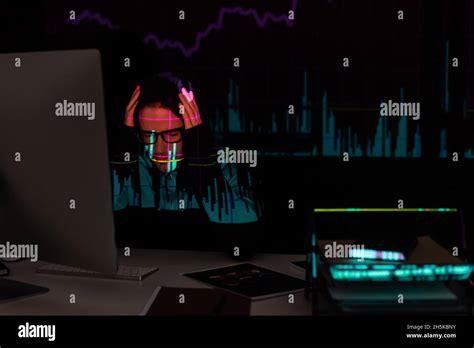 upset hacker with charts reflection sitting near computer and documents