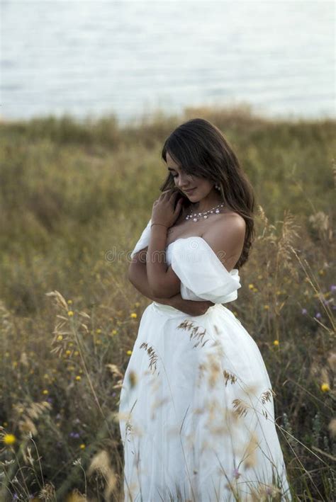 Elegant Girl In Long White Dress With Dark Long Hair Posing Against Sky