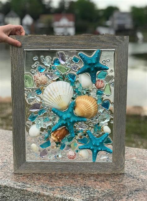 A Hand Holding Up A Glass Frame With Sea Shells And Seashells On It
