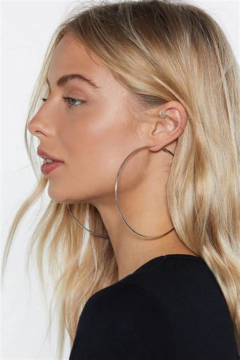 A Woman With Blonde Hair Wearing Large Hoop Earrings And A Black T Shirt Is Looking Away From