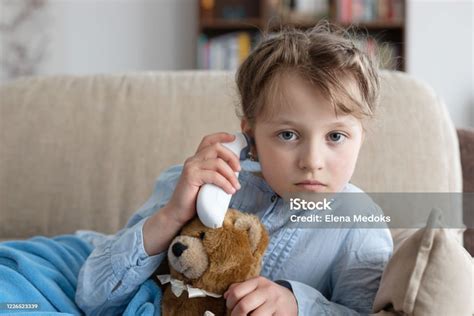 백인 귀여운 슬픈 소녀는 집에서 온도계와 그녀의 귀의 온도를 측정합니다 집에서 아픈 아이 발열 독감 감기와 독감에 대한 스톡