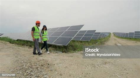 특수 균일 한 보행으로 태양 전지 패널을 검사하는 엔지니어 와 여성은 햇볕이 잘 드는 배터리 전기 엔지니어 환경의 설치에 대해 논의합니다 청정 에너지 생산 2명에 대한 스톡