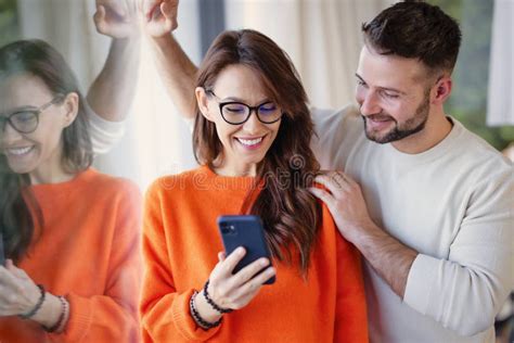 Happy Couple Standing Next To Eacht Other And Using Smartphone Stock