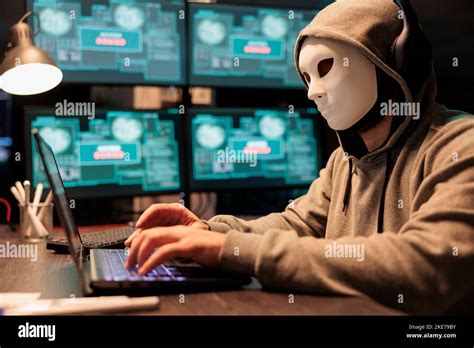 Impostor With Mask Hacking Computer Network At Night Working On Laptop