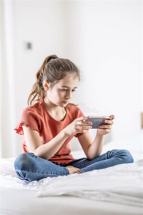 Young Addicted Gamer Girl Plays On A Phone While Sitting On A Bed At
