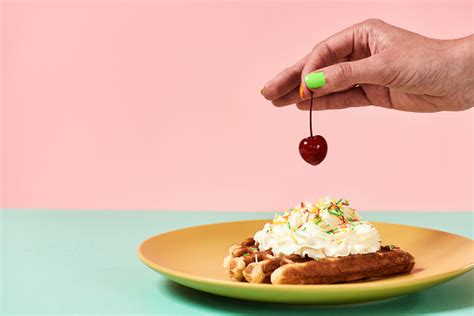 파스텔 핑크 그린 배경 위에 고립 된 접시에 휘핑 크림과 전통적인 벨기에 와플의 클로즈업 핸드 홀딩 및 체리 를 위에 추가