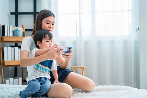 어머니는 스마트 폰을 사용하여 소셜 미디어를 열어 귀여운 작은 아들의 발달을 촉진합니다 18 23 개월에 대한 스톡 사진 및