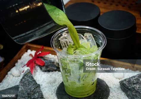일본 우유 말차 녹차 라떼를 붓고 검은 주전자에서 돌과 붉은 꽃으로 장식 된 아름다운 장식 쟁반에 얼음이 담긴 투명 플라스틱 컵에 퓨전 음료를 붓고 서빙 할 준비가되었습니다