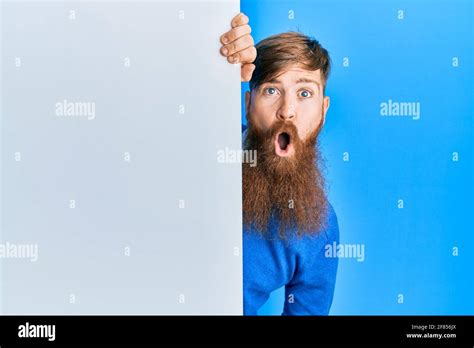 Young Irish Redhead Man Holding Blank Empty Banner Scared And Amazed