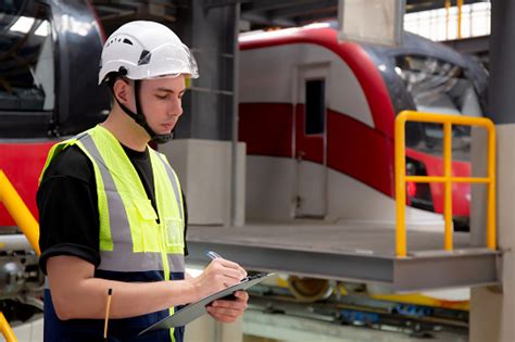 젊은 엔지니어 또는 노동자는 역 운송 및 인프라에서 유지 보수 및 클립보드에 문서 작성을 위해 전기 열차를 점검하고 검사관이