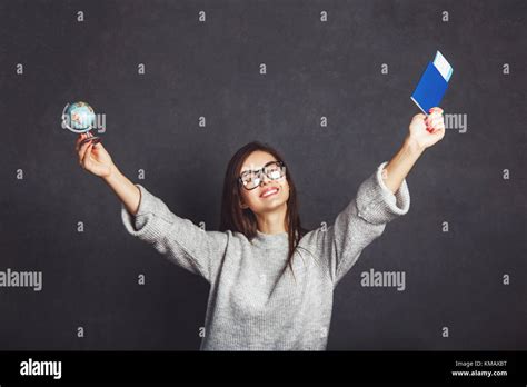 Cheerful Girl Holding Passport Plane Ticket And Globe Before Grey