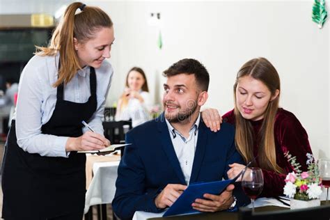 Welcoming Female Waiter Is Taking Order From Couple In Restaurante