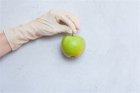 고무 장갑을 낀 손에는 녹색 사과 열매가 있습니다 녹색 사과는 밝은 회색과 흰색 현대 콘크리트 배경에 흰색 일회용 고무 라텍스