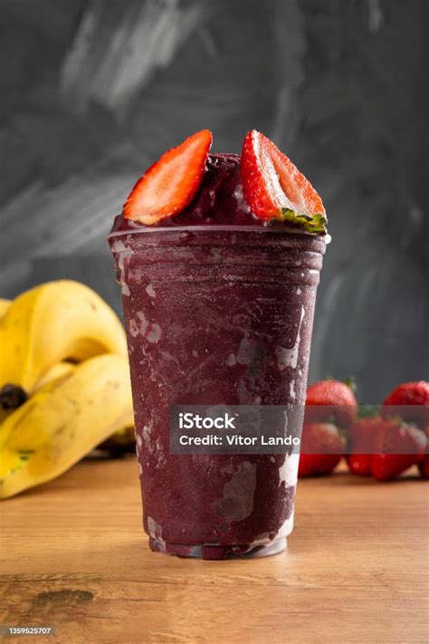 브라질 냉동 아사이 베리 아이스크림 스무디 에 플라스틱 컵 딸기 나무 책상과 과일이 있는 회색 여름 배경에 있습니다 메뉴 및 소셜 미디어에 대한 전면 보기 아사이에 대한