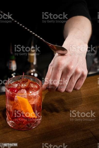 바텐더는 Negroni 알코올 칵테일 한 방울을 손에 얹고 맛 봅니다 바텐더는 바에서 클래식 네그로니 칵테일을 준비합니다 감귤류