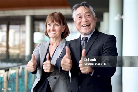 백인 사업가와 함께 양복을 입고 사무실에서 카메라를 향해 엄지손가락을 치켜세우는 행복한 미소 직장에서 성공한 노인 남성과 여성