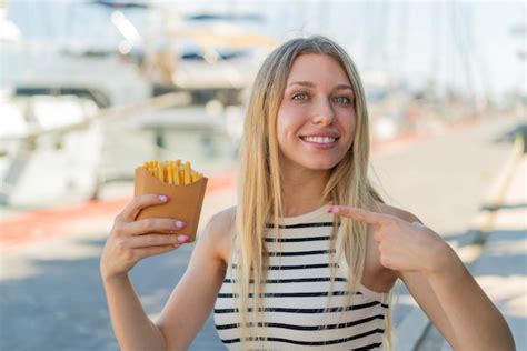 Premium Photo Young Blonde Woman Holding Fried Chips At Outdoors And Pointing It
