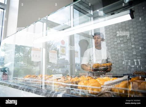 Male Baker Arranging French Pastries In Bakery Display Case Stock Photo