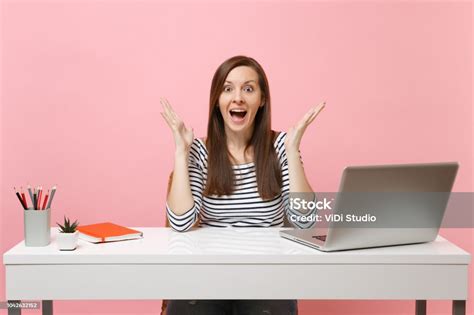 캐주얼 옷에 흥분된 여자 손을 확산 파스텔 핑크 배경에 고립의 현대 Pc 노트북과 일 흰색 책상에 앉아 성과 비즈니스 경력