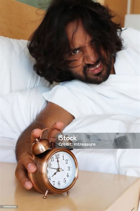 심술궂은 인도 남자가 호텔 더블 침대를 가로질러 손을 뻗는 클로즈업 이미지 침대 옆 탁자에 알람 시계를 끄고 청동 금속 케이스 복고풍 알람 시계 더블 벨 아날로그 디스플레이