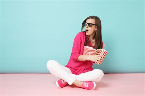 장미 셔츠 밝은 분홍색 파란 파스텔 벽 배경 스튜디오에 고립 된 영화 필름을 보고 바닥에 앉아 흰색 바지에 전체 길이 초상화