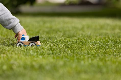 공원의 녹색 잔디에 장난감 케이와 함께 노는 아이의 손의 클로즈업 작은 차를 가지고 노는 유아 소년 보육 및 보육 야외 어린