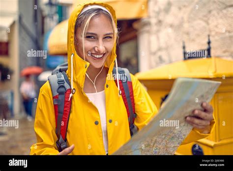 Young Girl With A Yellow Raincoat And Map On The Street While Enjoying