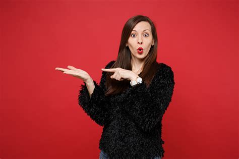 검은 모피 스웨터 포인팅 검지 손가락 손 옆으로 스튜디오에서 밝은 빨간 벽 배경에 고립에 충격된 젊은 여자의 초상화 사람들이 진심으 감정 라이프 스타일 개념 복사 공간을