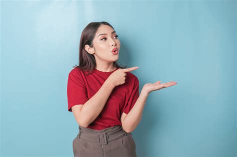 파란색 배경으로 격리된 그녀 옆의 복사 공간을 가리키는 빨간 티셔츠를 입은 충격을 받은 아시아 여성 25 29세에 대한 스톡 사진 및 기타 이미지 Istock