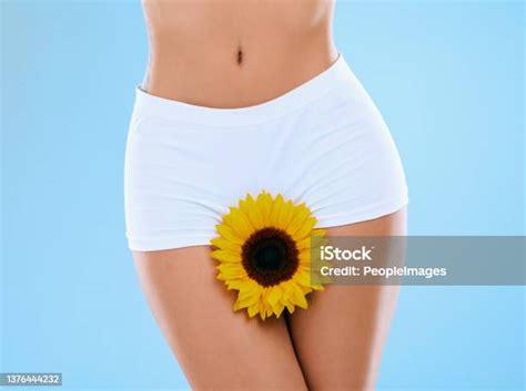 파란 배경을 향해 포즈를 취하는 동안 허벅지 사이에 꽃을 들고 있는 인식할 수 없는 여성의 스튜디오 샷 요로감염에 대한 스톡