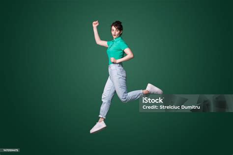 녹색 배경 위에 고립된 충격적인 얼굴 표정으로 점프하는 젊은 여성의 전신 프로필 측면 사진 점프에 대한 스톡 사진 및 기타