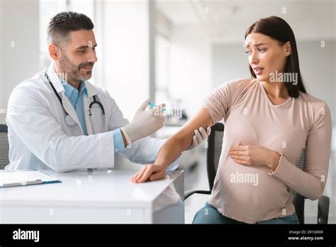 Young Pregnant Woman Scared Of Vaccine Injection Looking At Syringe