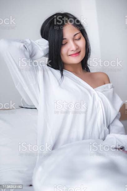 아름 다운 젊은 예쁜 아시아 여자 일어나서 아침에 흰색 침대에서 흰색 셔츠와 함께 행복 한 미소를 확인 매트리스에 대한 스톡